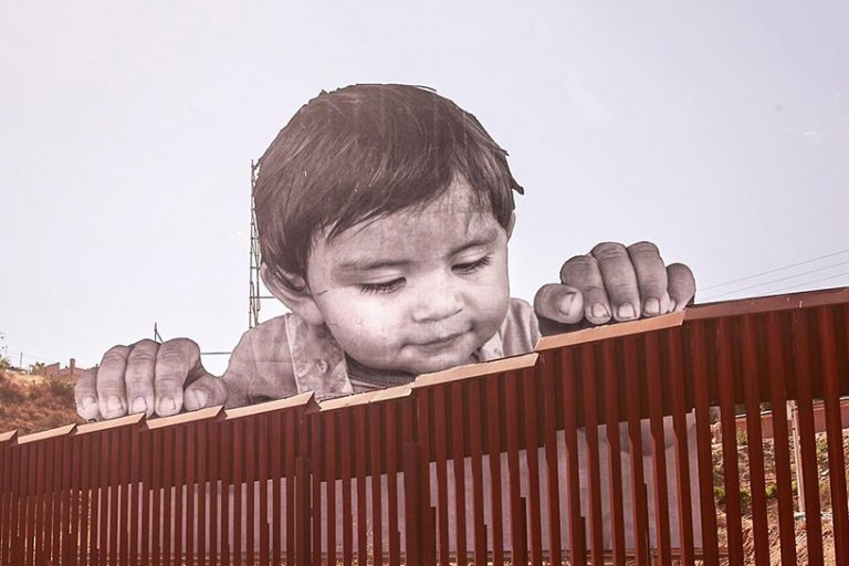 child curiously peeks over the US-mexico border in JR installation