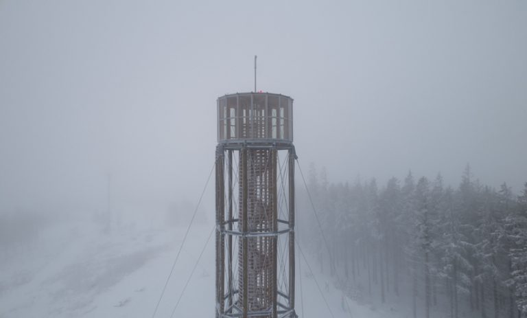 a lookout tower rises above the forested mountains of a czech ski area