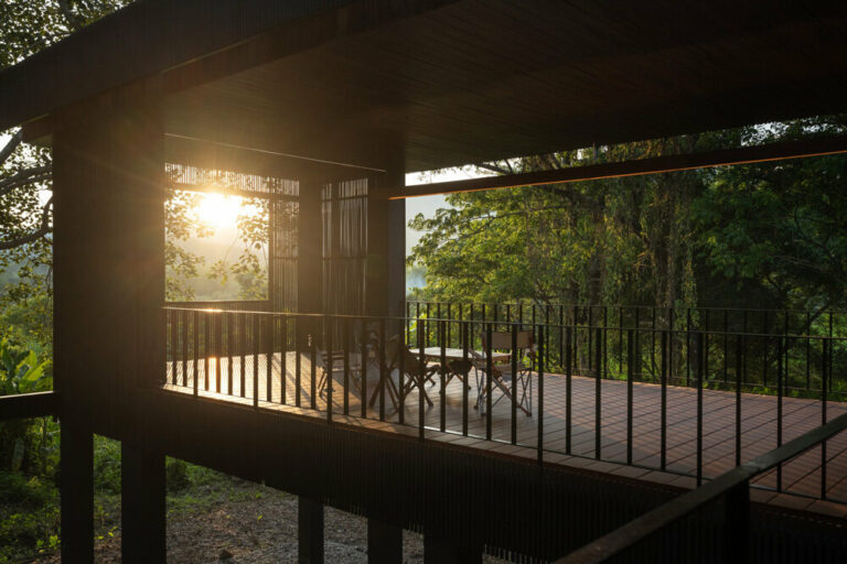 timber-clad residence settles on stilts within raintree forest in thailand