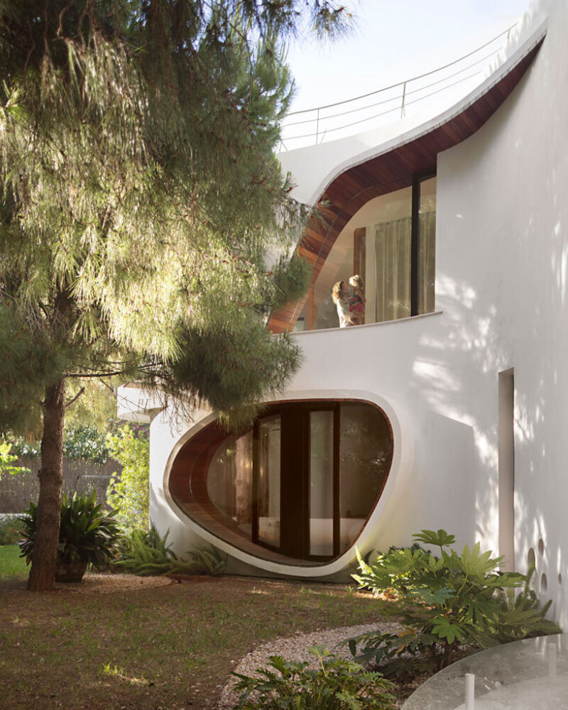 organic residence's curved white planes emerge from lush greenery in spain